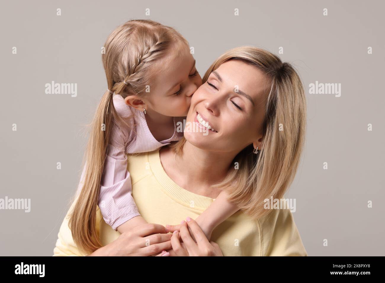 Daughter kissing her happy mother on grey background Stock Photo - Alamy