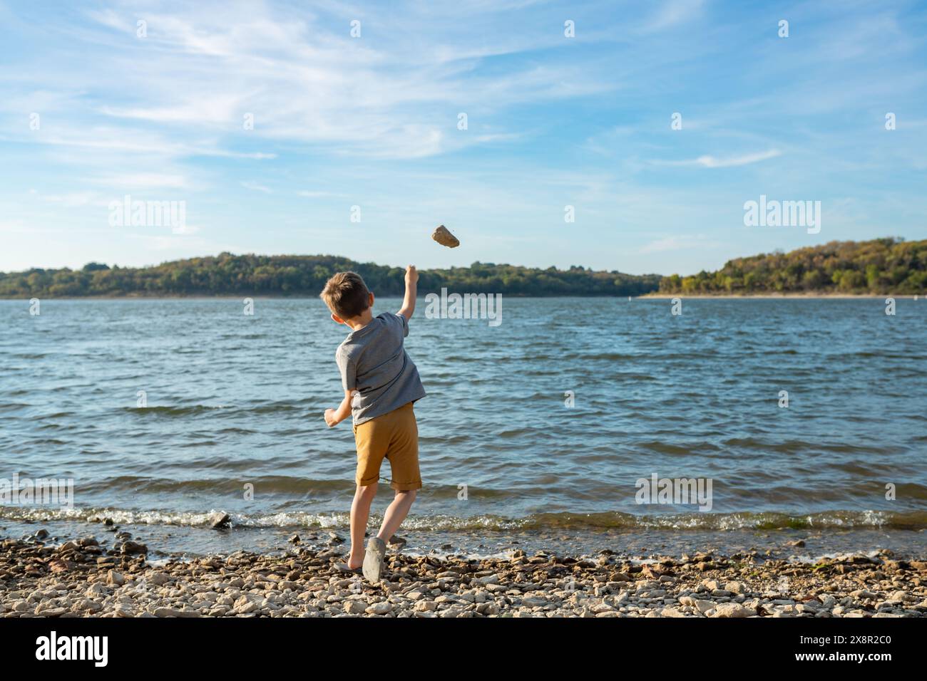 young boy throws rock into lake with waves on a sunny day Stock Photo ...