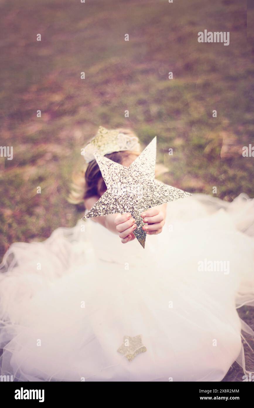 Girl in white dress holding a glittery star, sitting on the gras Stock ...