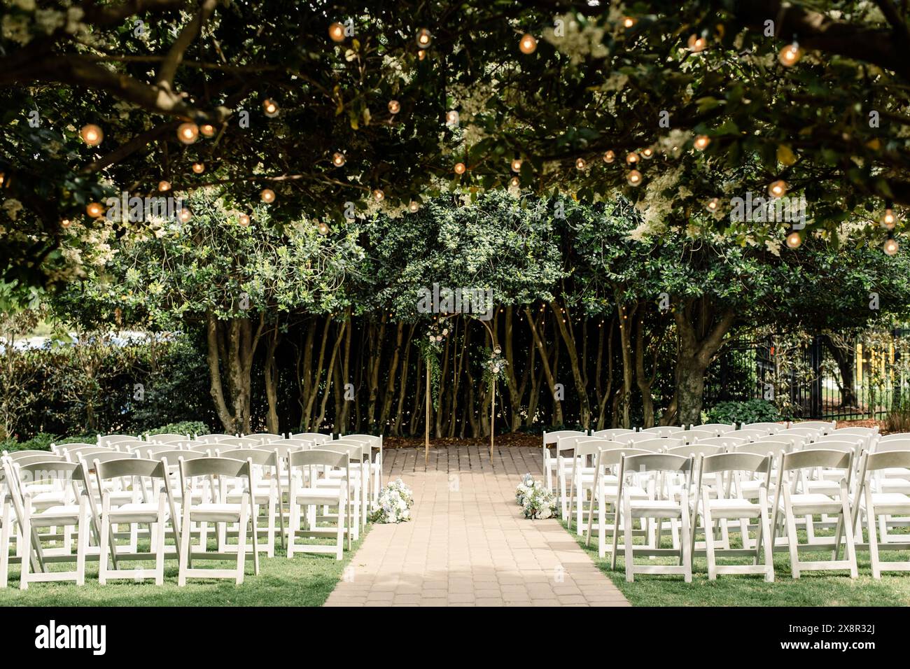Outdoor wedding ceremony setup with white chairs and string lights ...