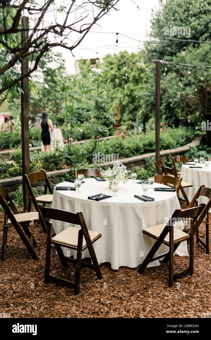 Outdoor garden reception setup with round tables and wooden chairs ...