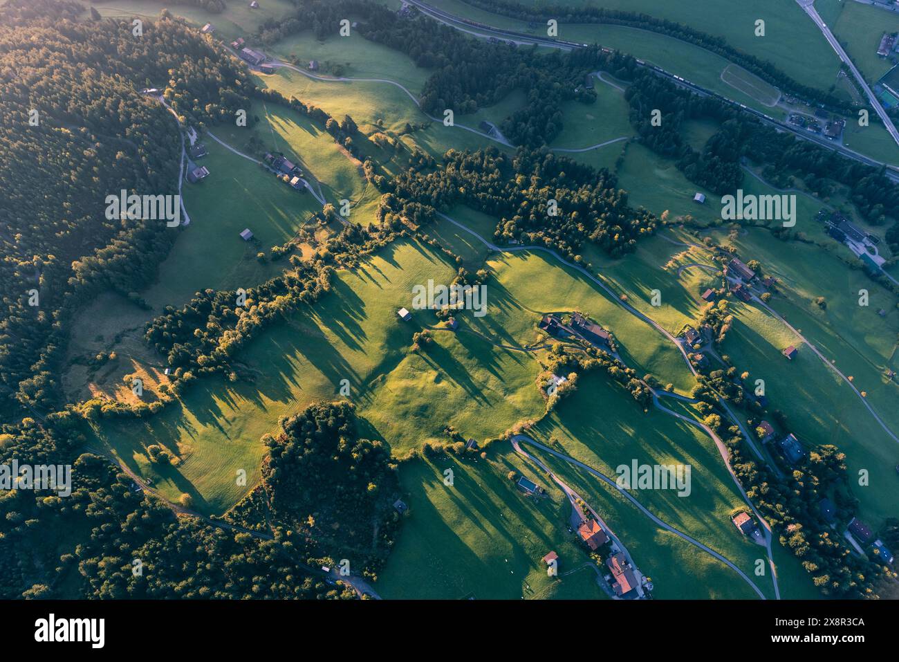 Aerial view, Green meadows, tree shadows, winding roads below Stock ...