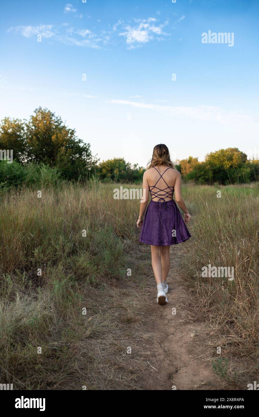 Sixteen-year-old girl in a purple dress walking gracefully in a field ...