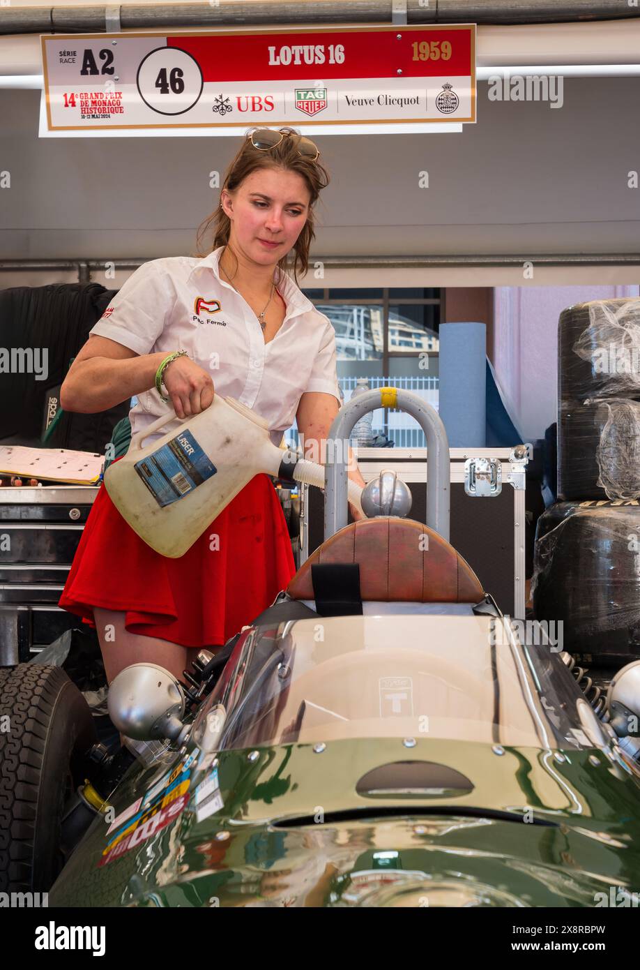 Pretty woman in a red skirt filling a classic racing car with fuel at ...