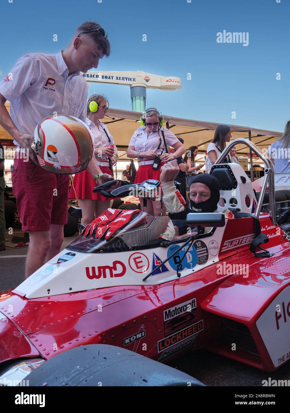 A man and two women in red preparing a red Surtees TS9B classic racing ...