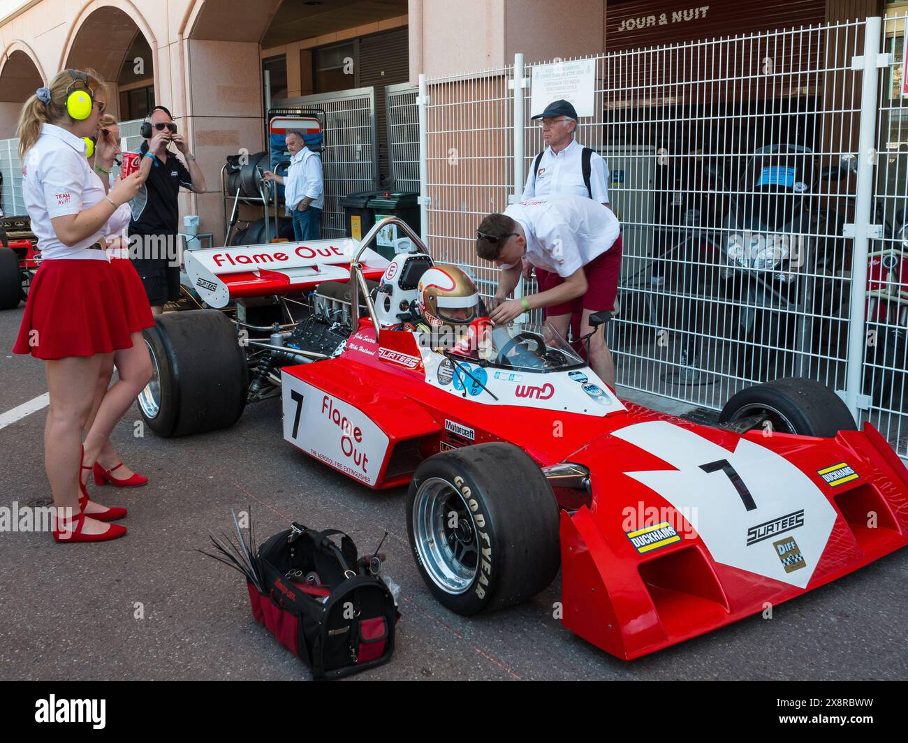 A man and two women in red preparing a red Surtees TS9B classic racing ...