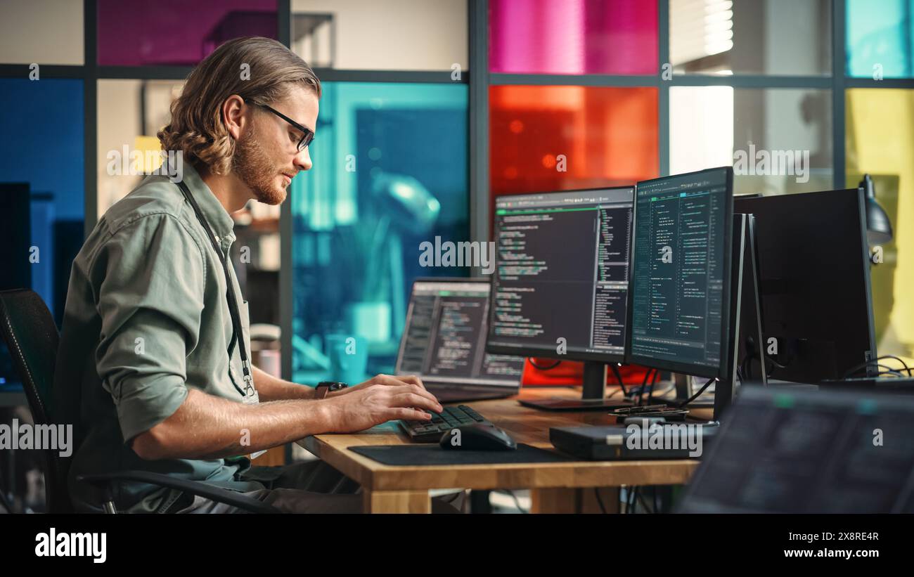 Male Programmer Writes Code On Desktop Computer With Multiple Monitor Setup And A Laptop Aside