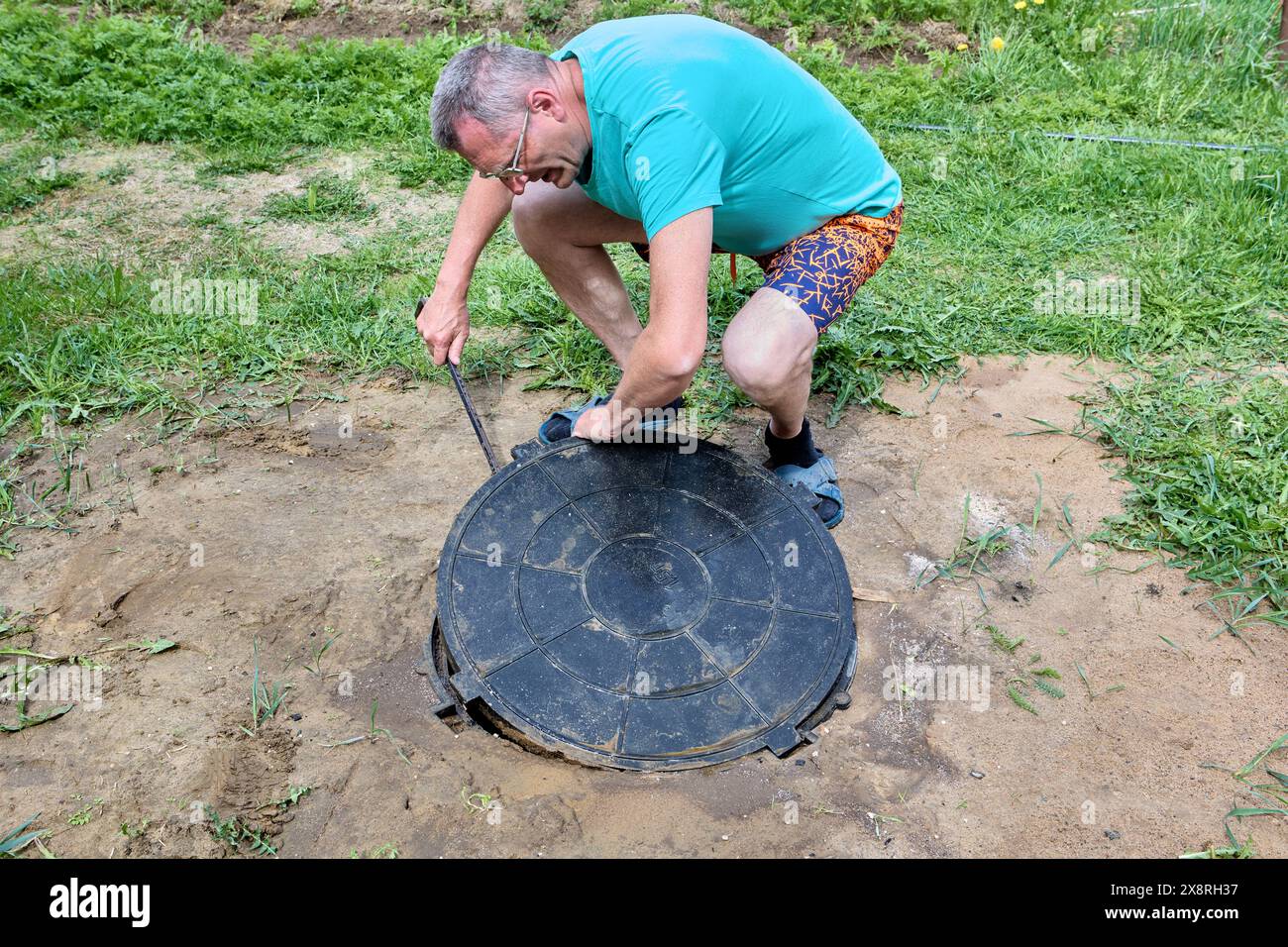Man lifts manhole cover with crowbar to service drainage well Stock ...
