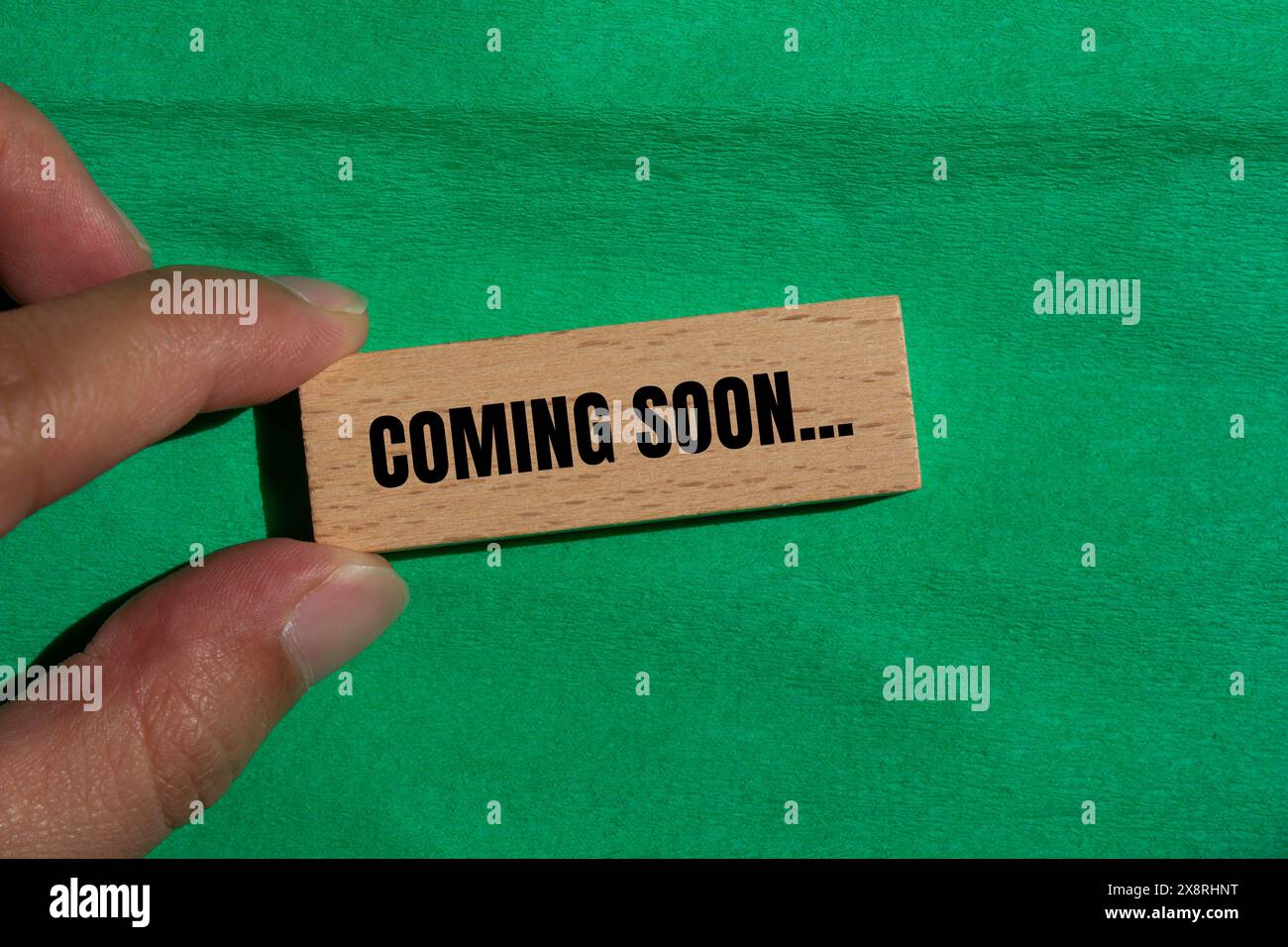 Coming soon words written on wooden block with green background ...