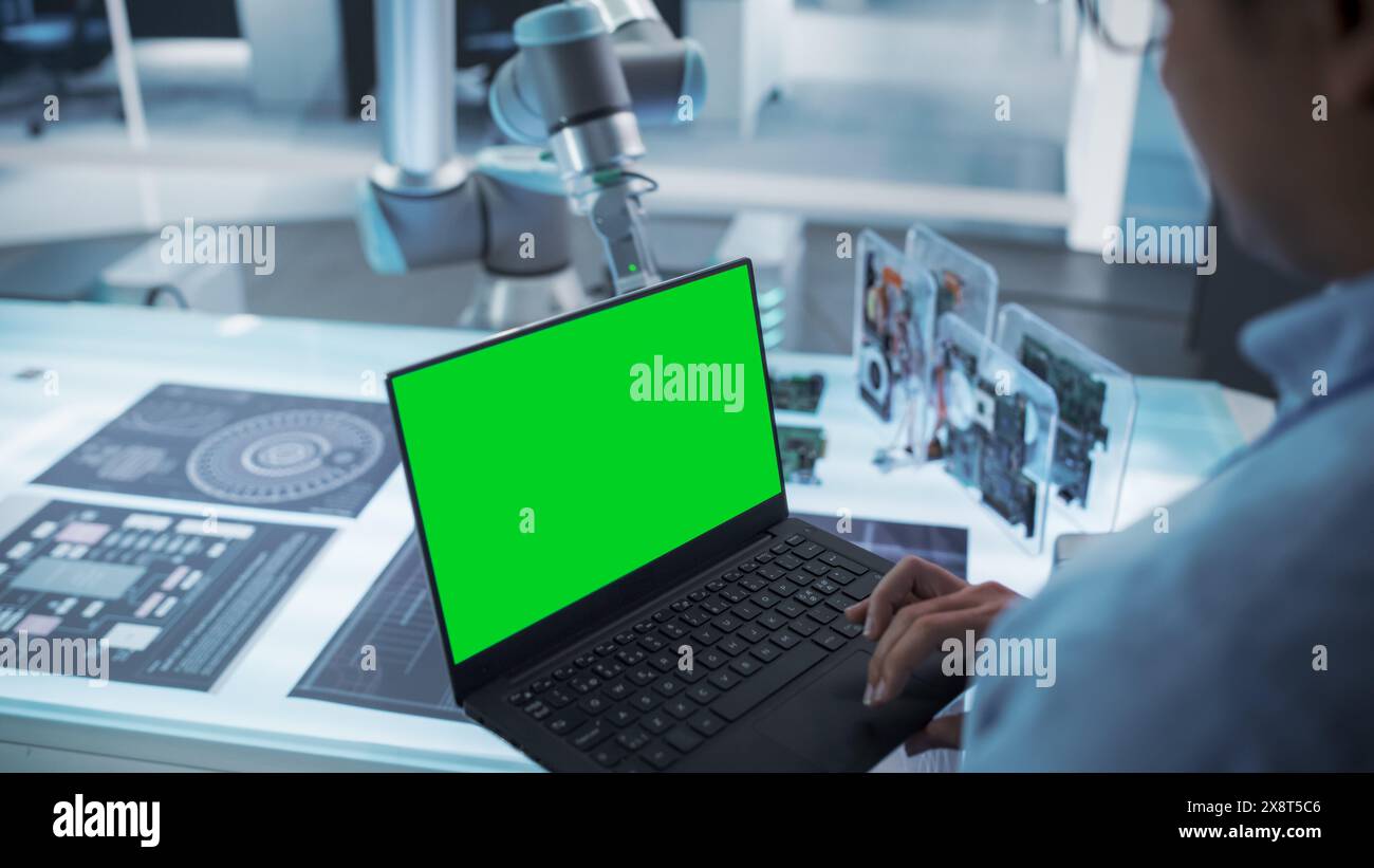 Over the Shoulder Shot of a Robotics Engineer Using a Laptop Computer with Green Screen Mock Up ...