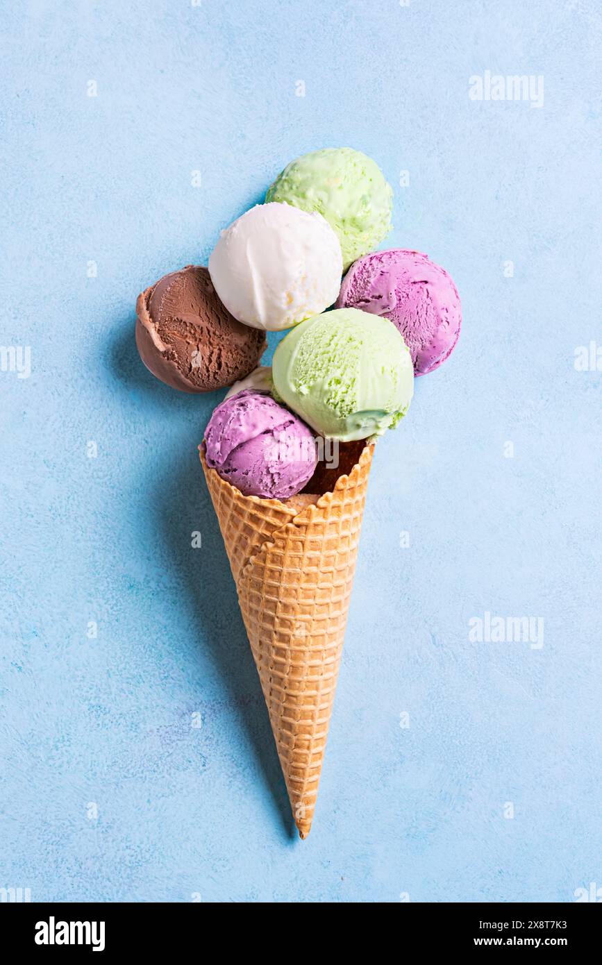 Ice cream cone with various scoops on blue background, creative flat lay. Many organic colourful ...