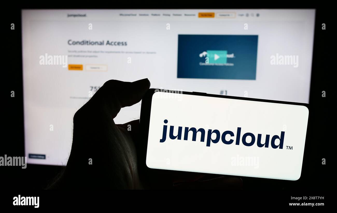 Person holding mobile phone with logo of American cloud software company JumpCloud Inc. in front ...