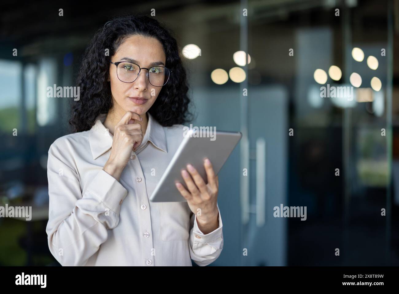 A professional Hispanic woman with curly hair and glasses is focused on ...