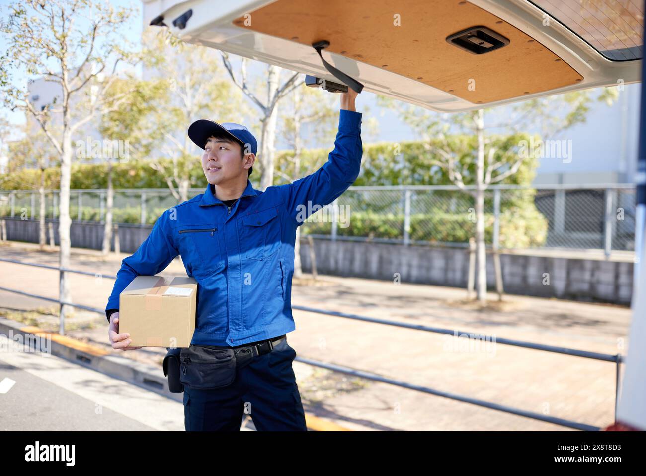 Japanese delivery man holding a box and standing next to a van Stock ...