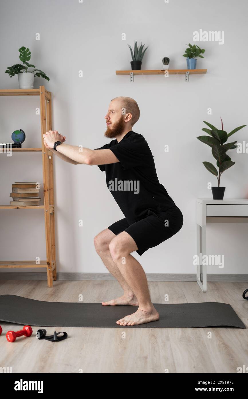 Sporty young man doing squat exercise in living room, crouching ...