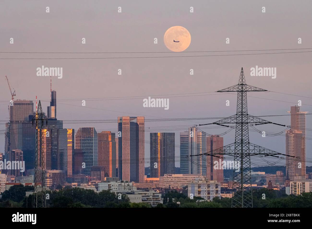 The full moon passes over the Frankfurt banking skyline as an aeroplane ...