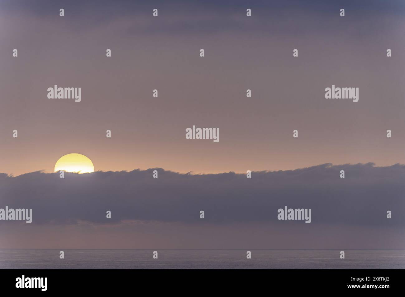 A serene sunrise over the ocean horizon, with the sun partially hidden ...