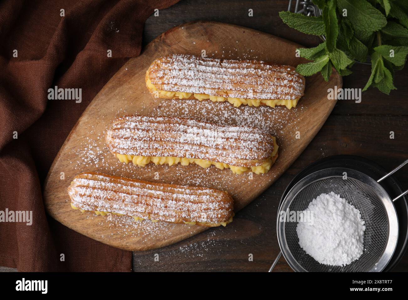 Delicious eclairs filled with cream, mint and powdered sugar on wooden ...