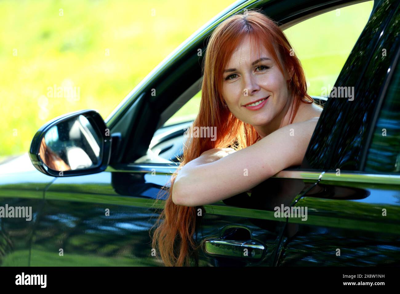 A girl poses for the camera with her car in nature. Joy, happiness ...