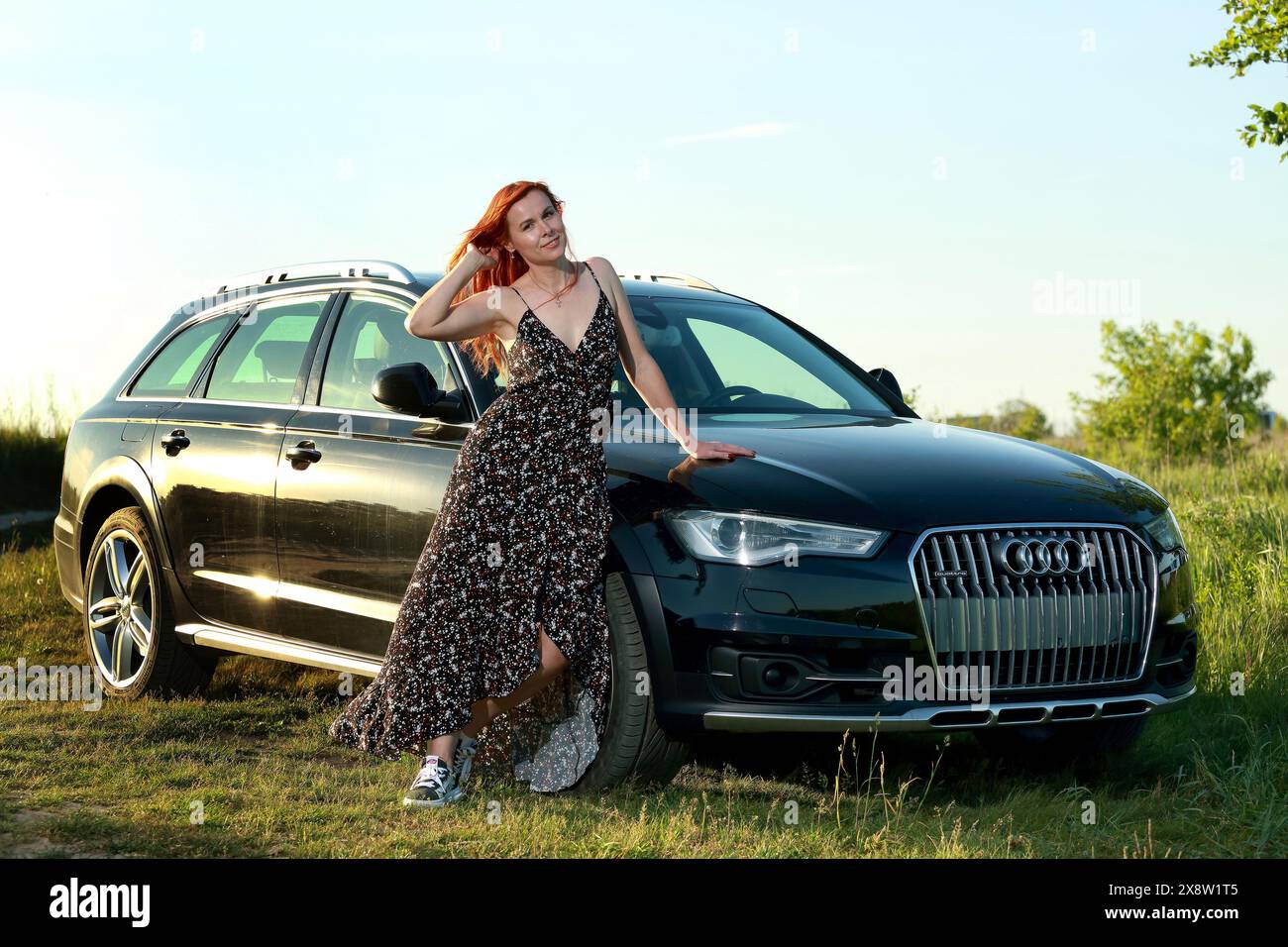 A girl poses for the camera with her car in nature. Joy, happiness ...