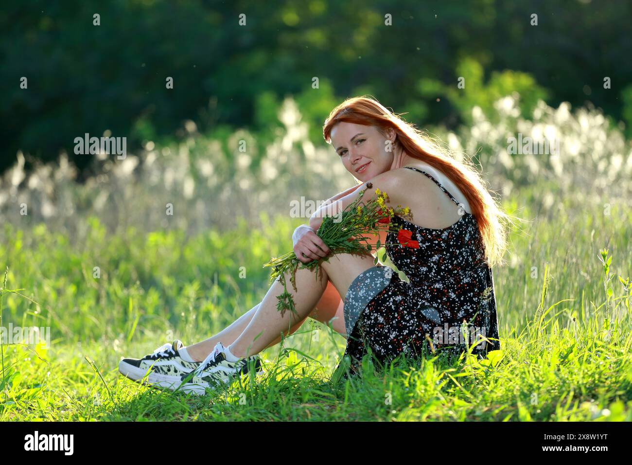 A girl in a red blouse and white jeans poses for the camera in nature ...