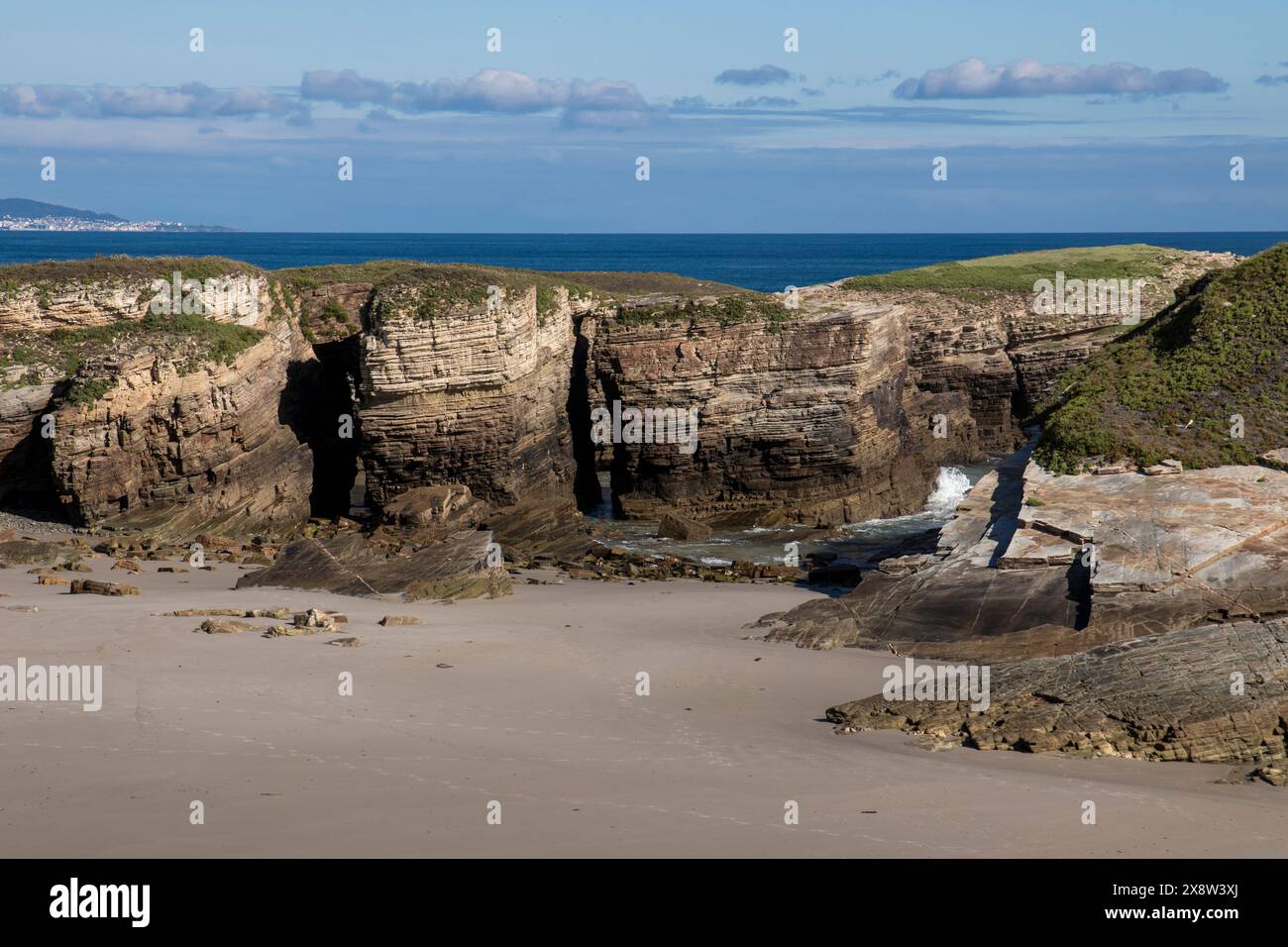 coastal scene with layered rock cliffs, a sandy beach, and a clear blue ...