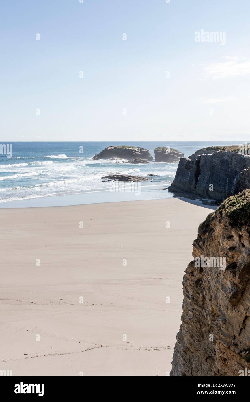 serene beach with cliffs, ocean waves, clear sky, and an isolated rock ...