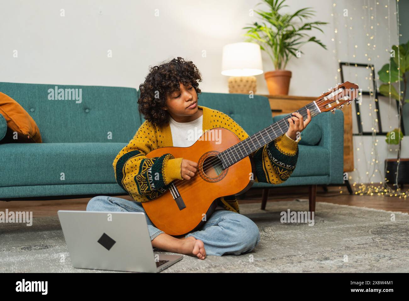 African American woman learning guitar watching tutorial on laptop at ...