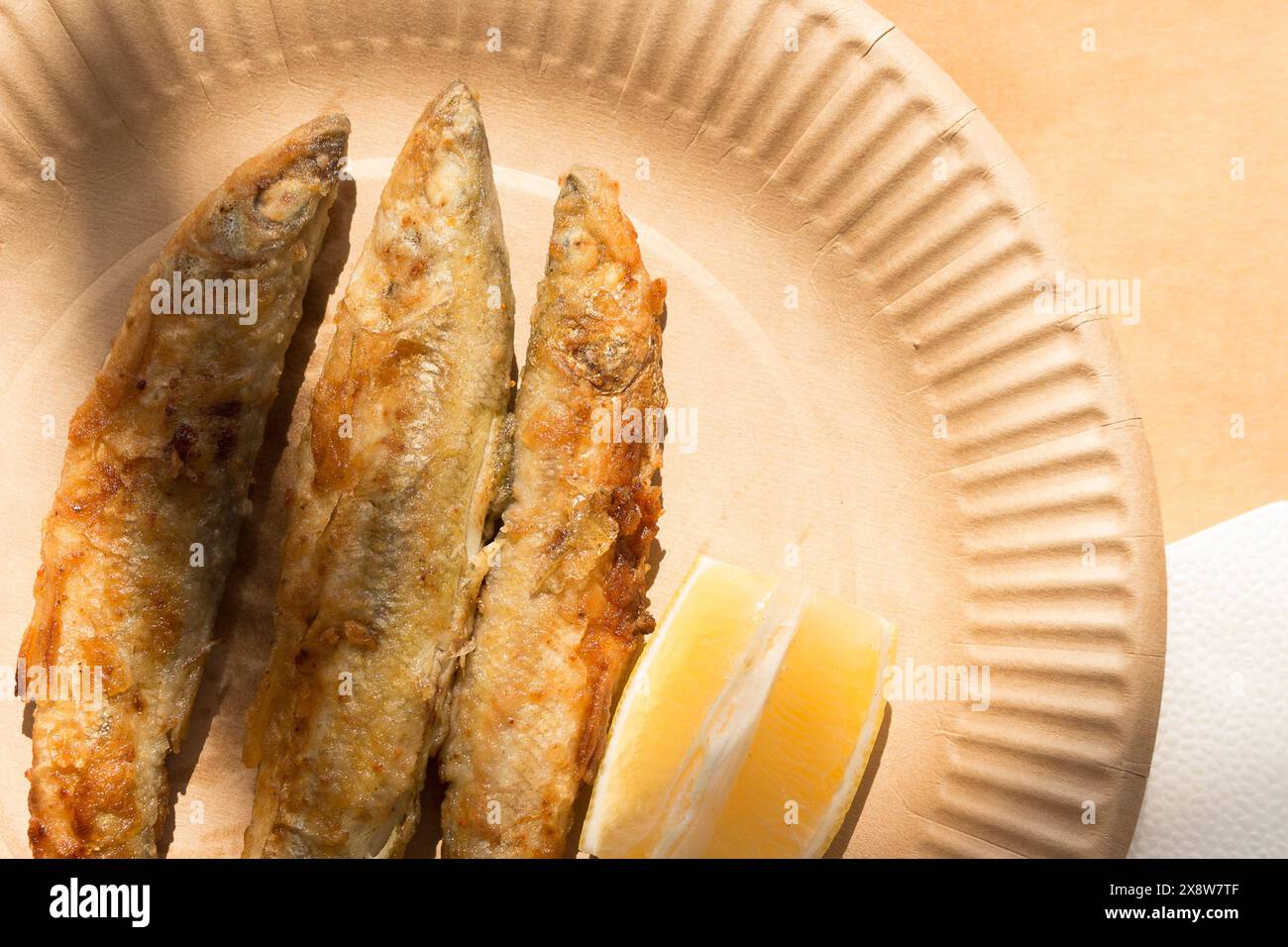 Delicious fried smelt on a cardboard plate with a slice of lemon, top ...