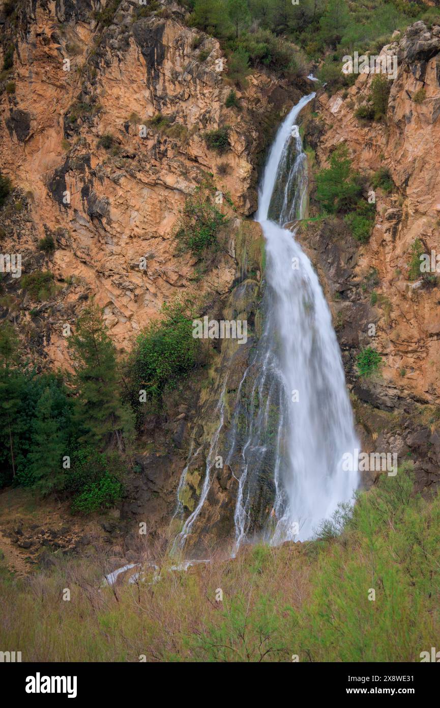 The image features a tall, cascading waterfall flowing down a rugged ...