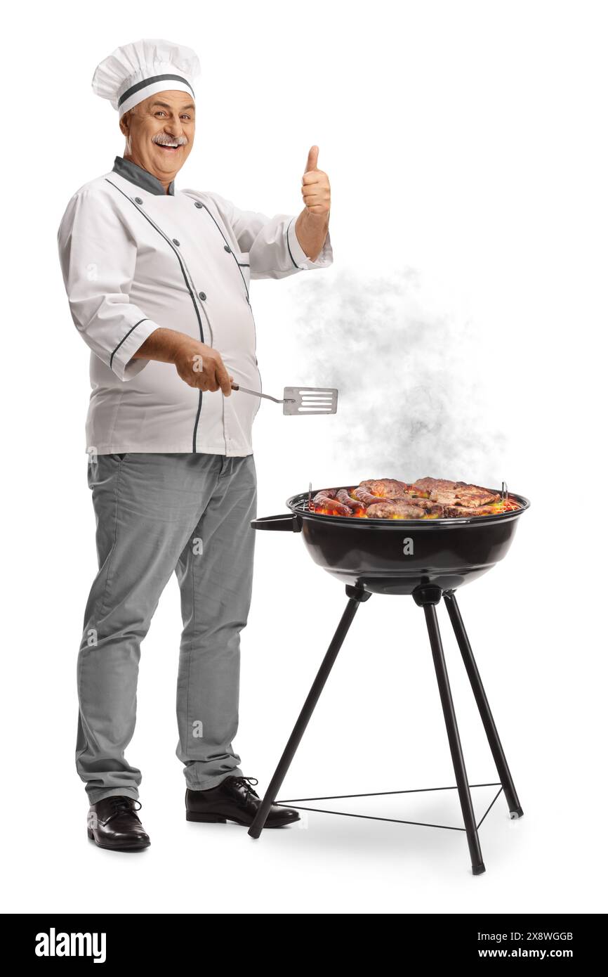 Mature male chef grilling meat on a bbq and gesturing thumbs up ...