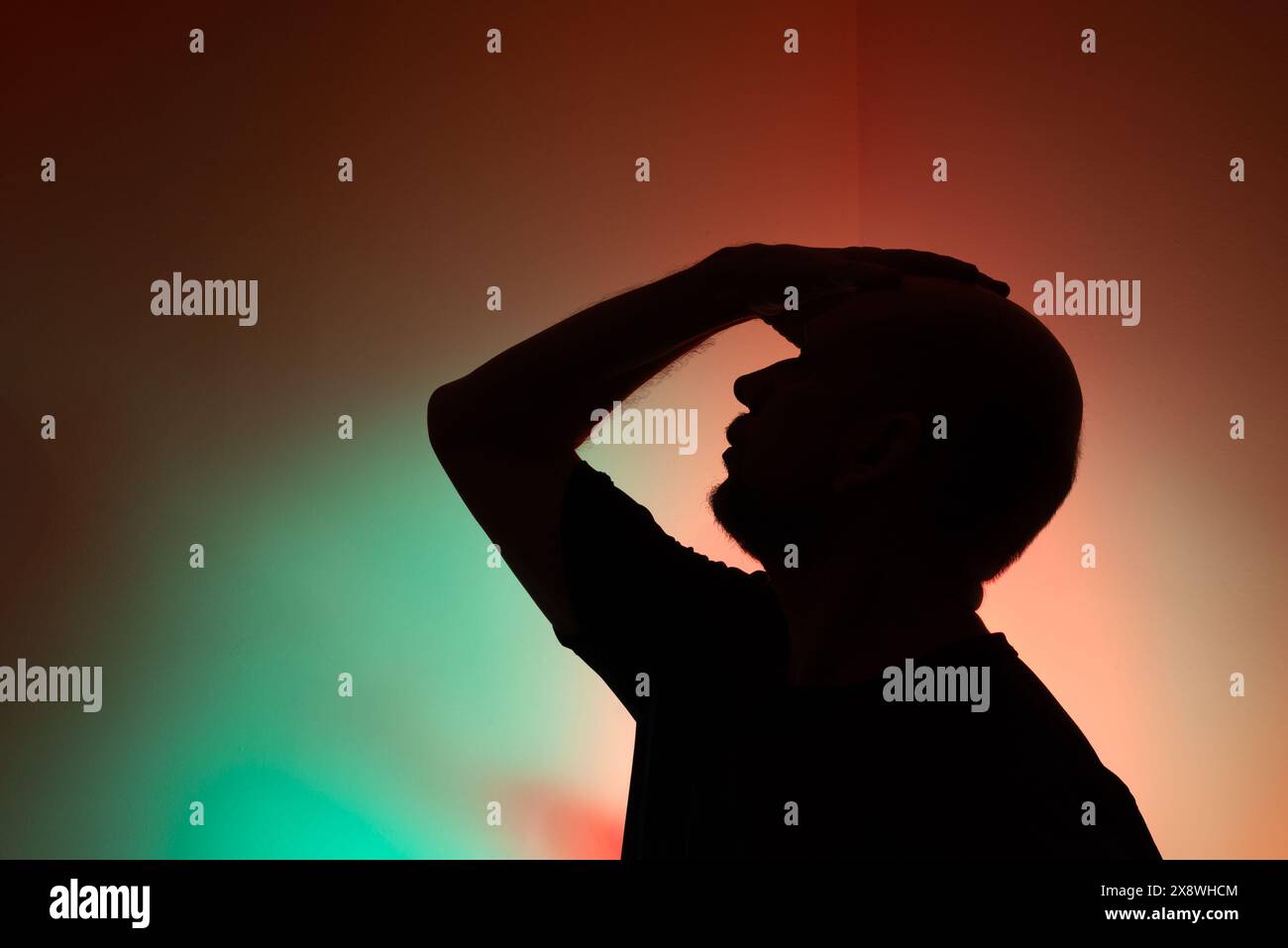 Studio portrait of a man in silhouette with his hand over his head ...