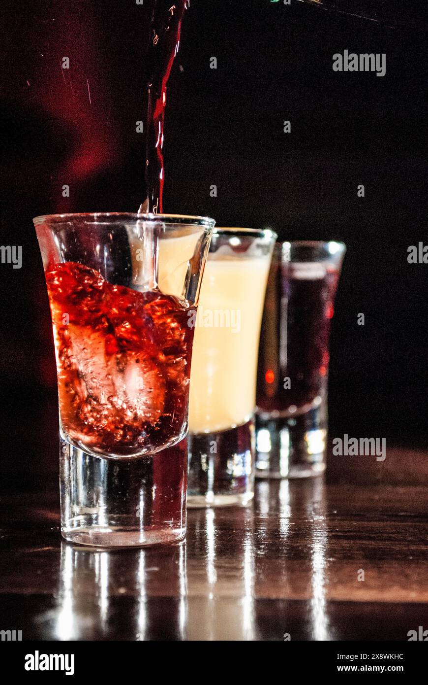 Three shot glasses filled with colorful drinks, one being poured, set ...