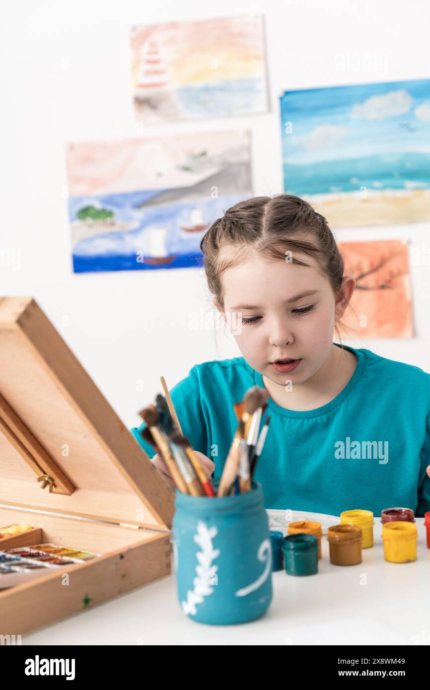 Little girl of pre-adolescence drawing on easel. Beautiful little girl ...