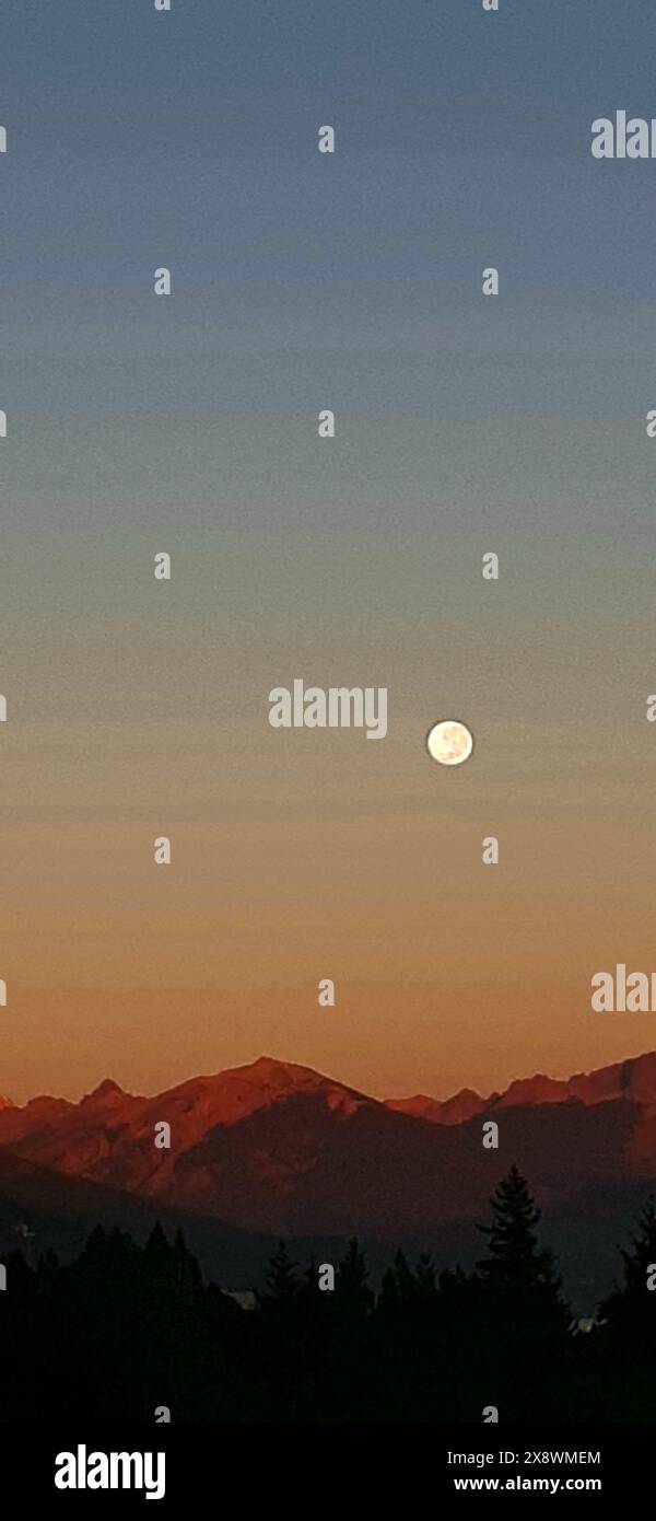 Full moon rising over a mountain range during twilight, with a gradient ...