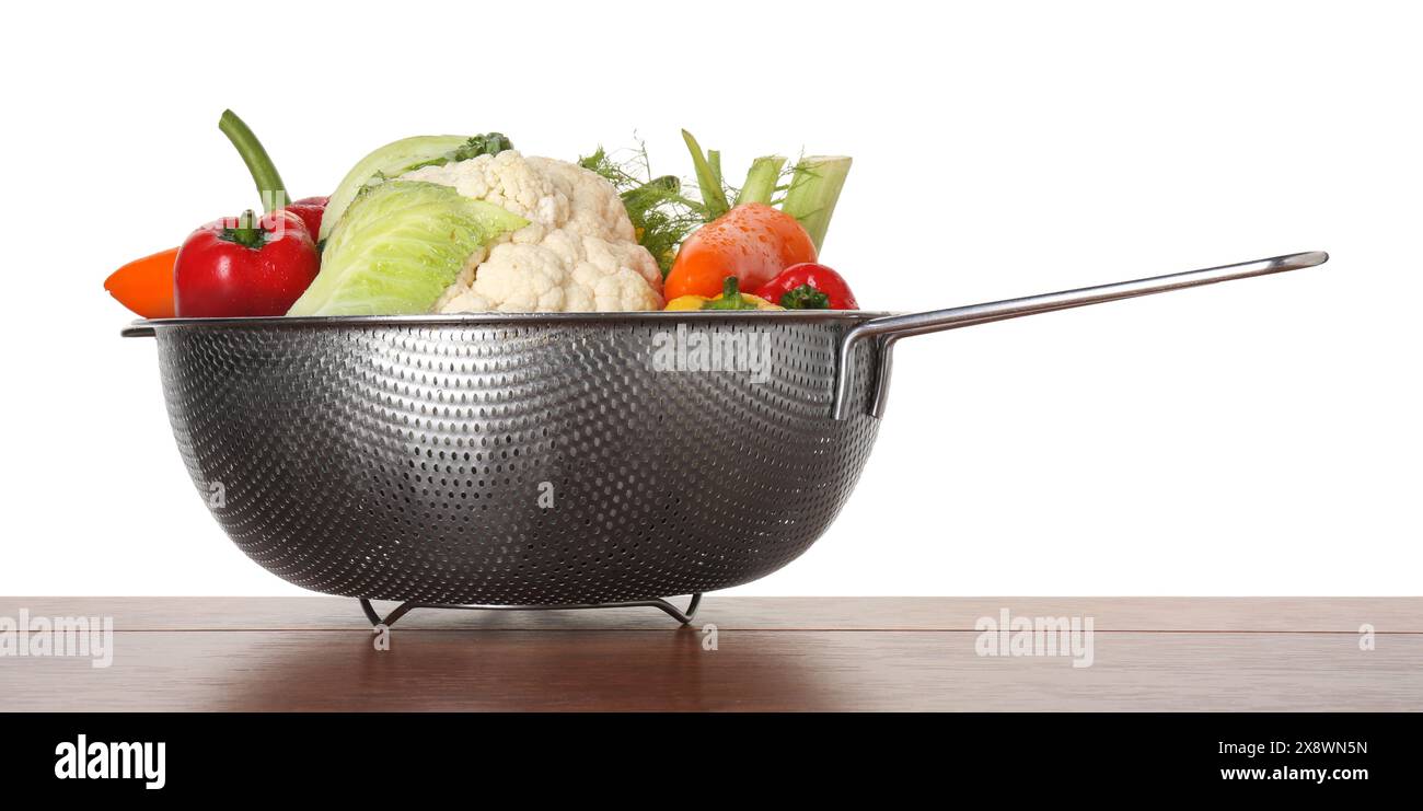 Metal colander with different vegetables on wooden table against white ...