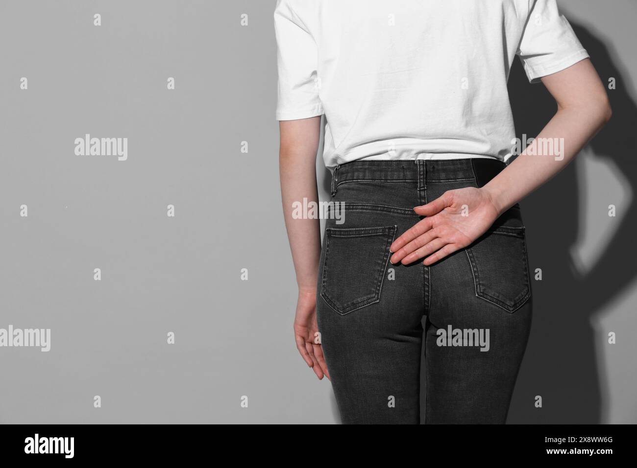 Woman showing open palm behind her back on grey background, back view ...