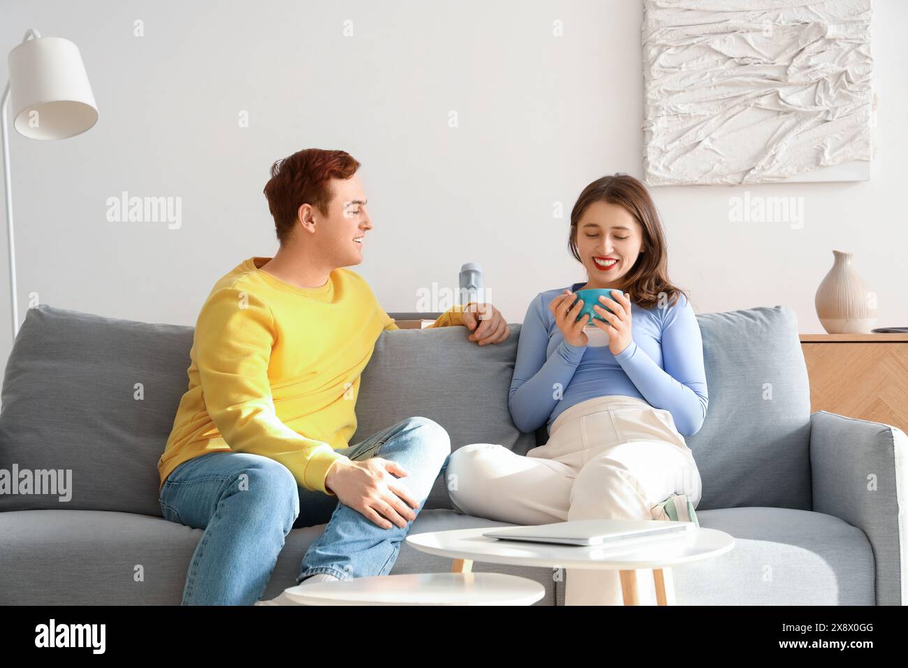 Young couple chatting on grey sofa at home Stock Photo - Alamy