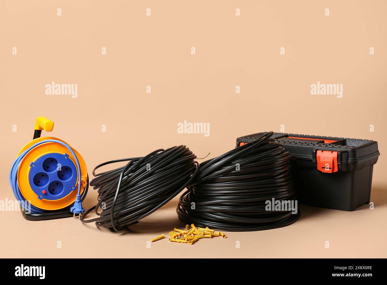 Rolled wires, wall plugs, tool box and extension cable reel on beige ...