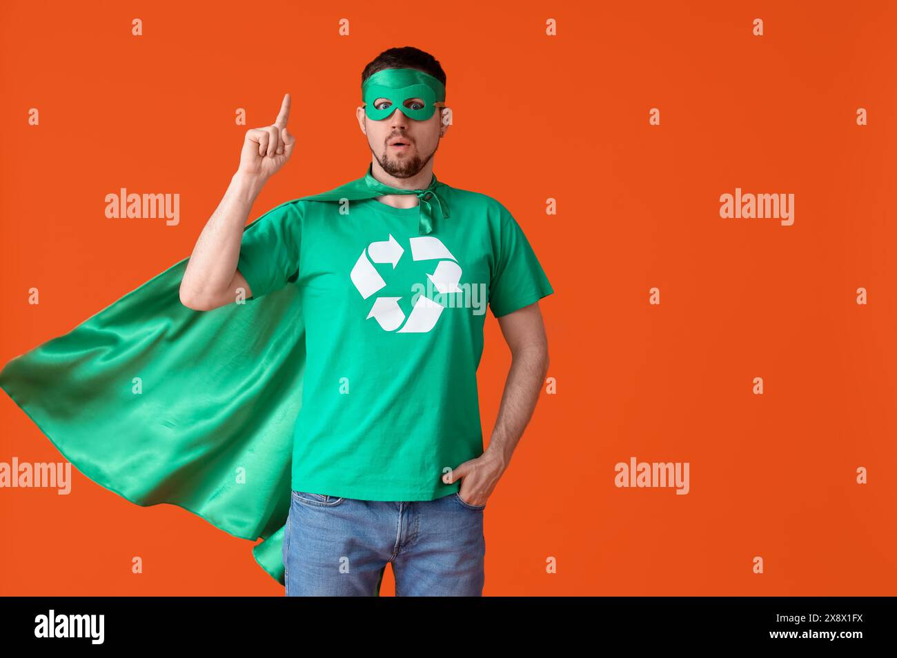 Surprised young man dressed as eco superhero pointing up on orange ...