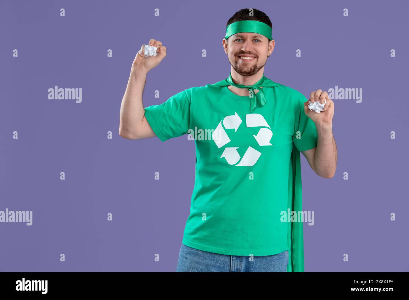 Young man dressed as eco superhero with rubbish on lilac background ...