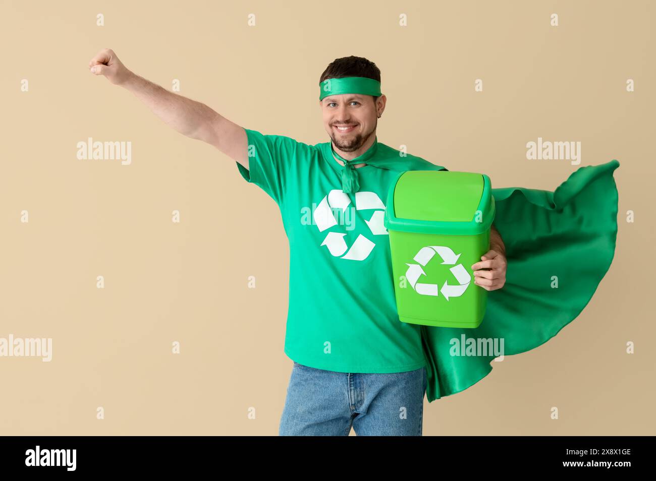 Young man dressed as eco superhero with garbage bin on beige background ...