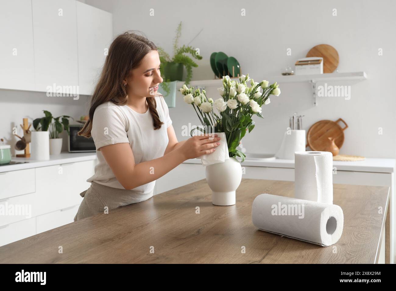 Young woman wiping flowers with paper towel in kitchen Stock Photo - Alamy