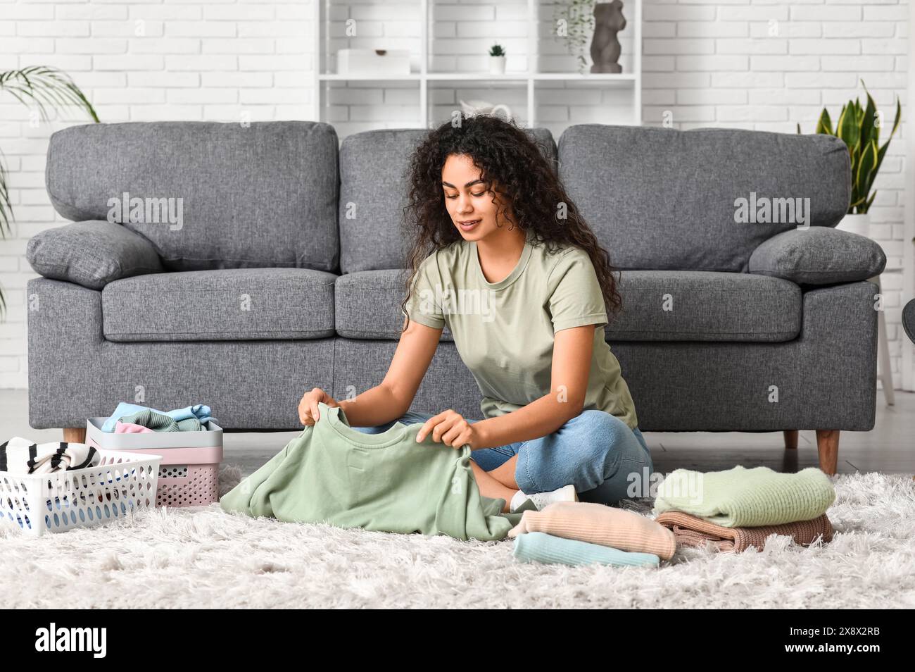 Beautiful young happy African-American woman folding clean clothes at ...