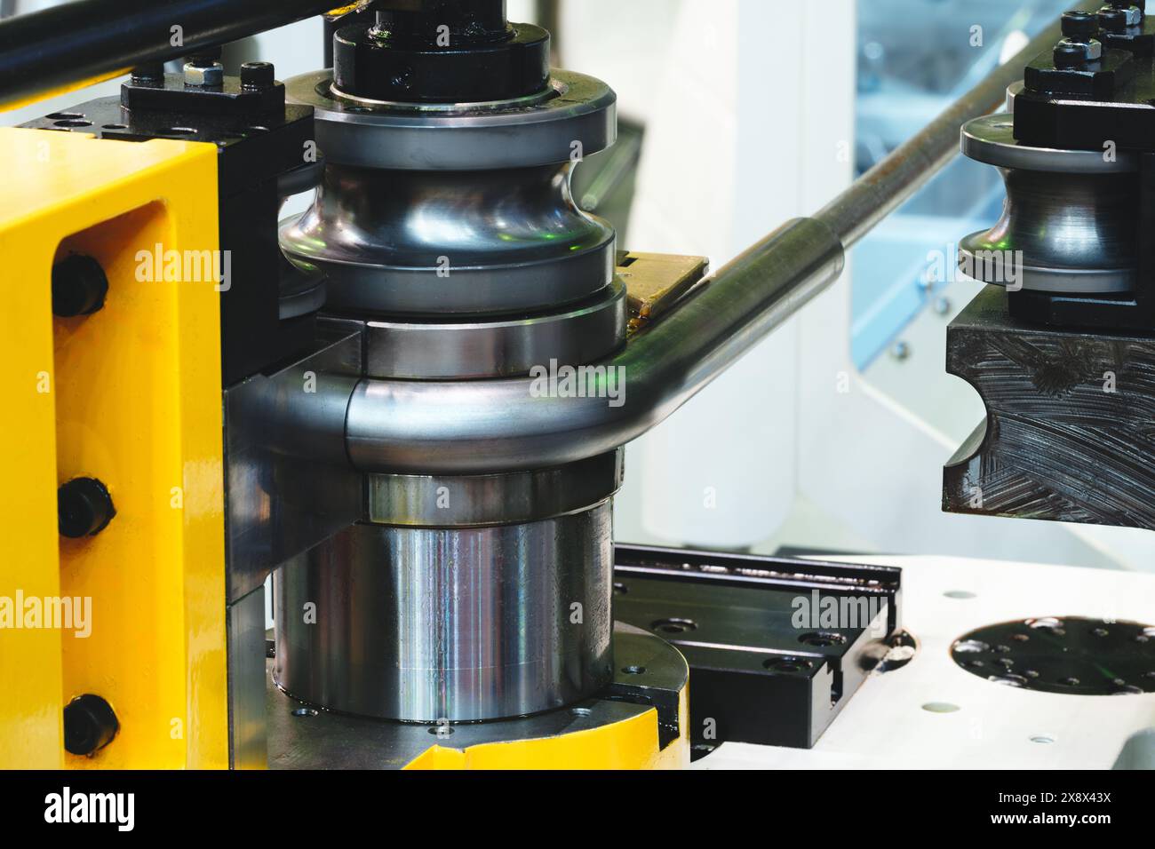 A machine is bending a metal pipe. The machine is yellow and black. The ...