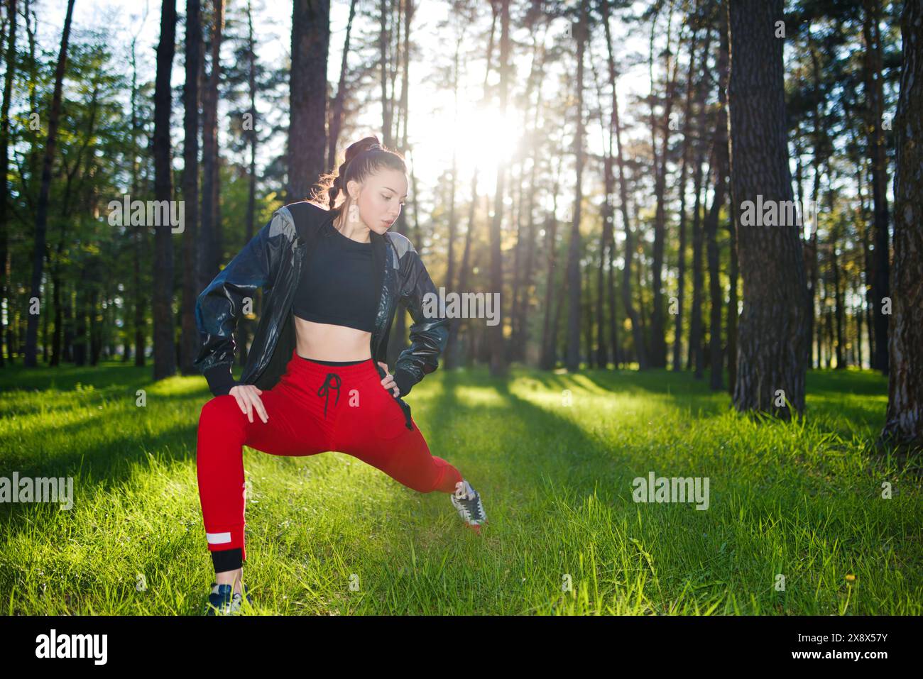 Young woman in tracksuit doing leg stretches in a park in early spring ...