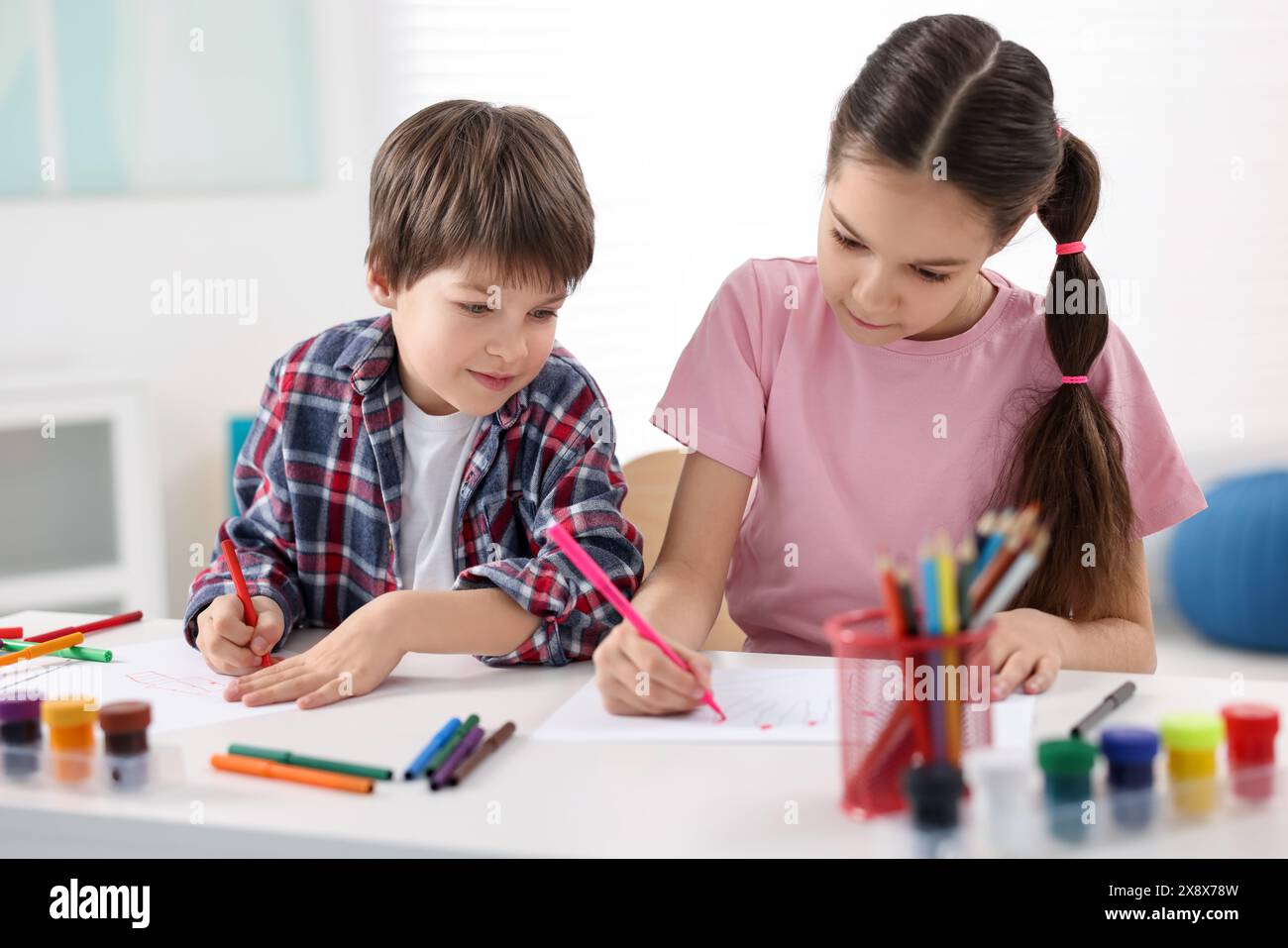Happy brother and sister drawing at white table in room Stock Photo - Alamy