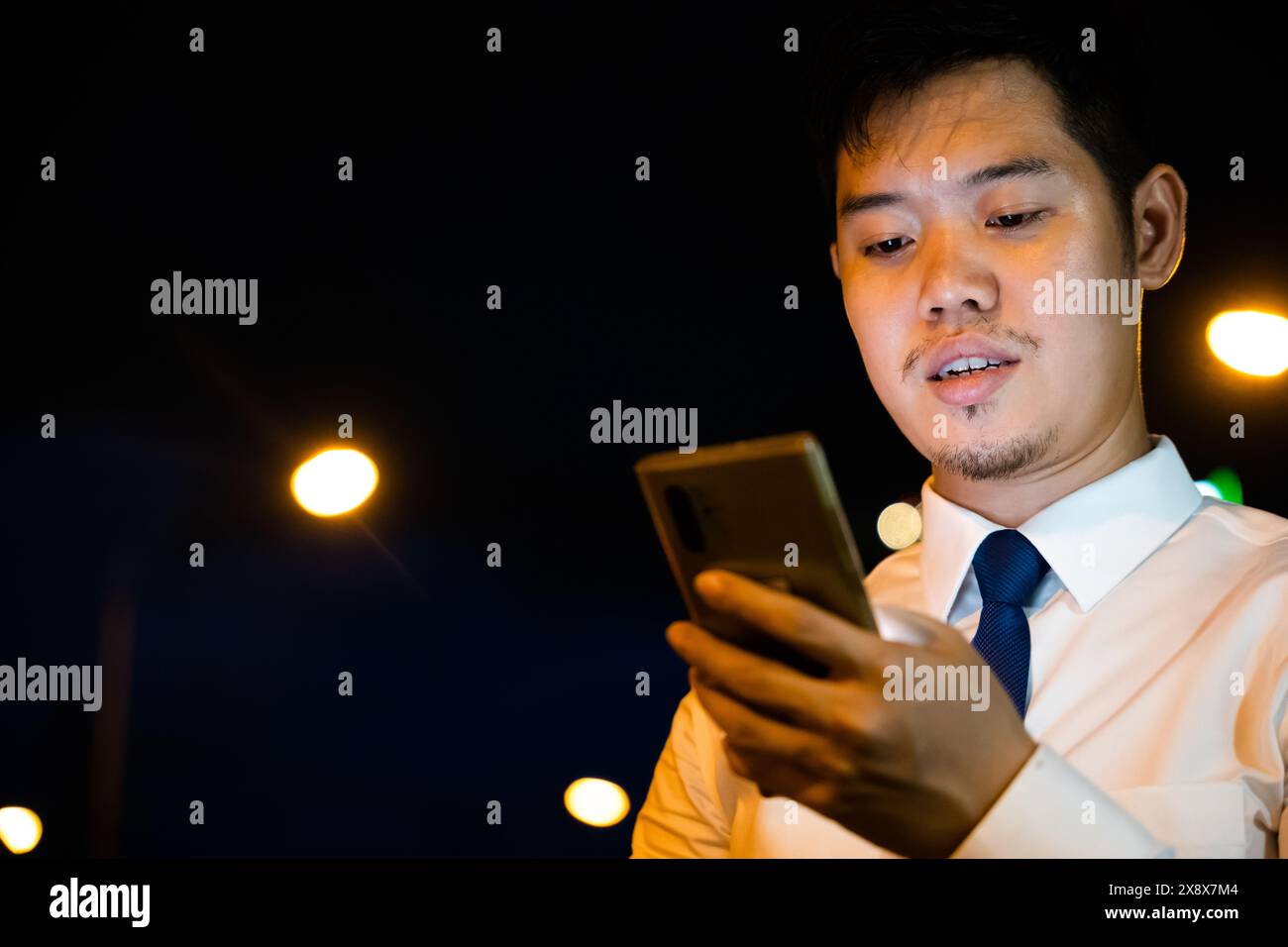 Man in suit using smartphone in vibrant city night. Engaged in social ...