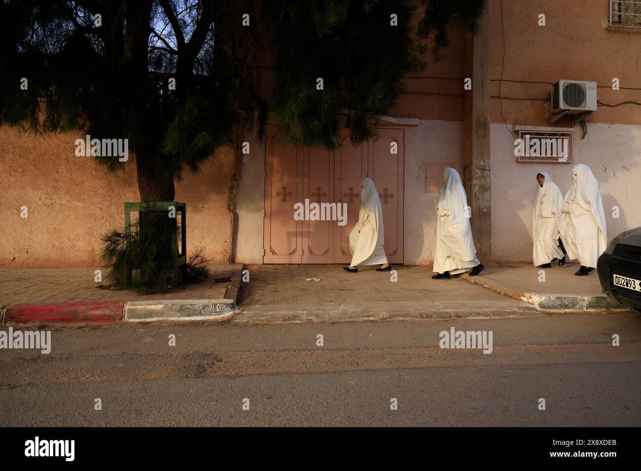 Veiled Mozabite women in white haik walking outside of Ksar El Atteuf ...
