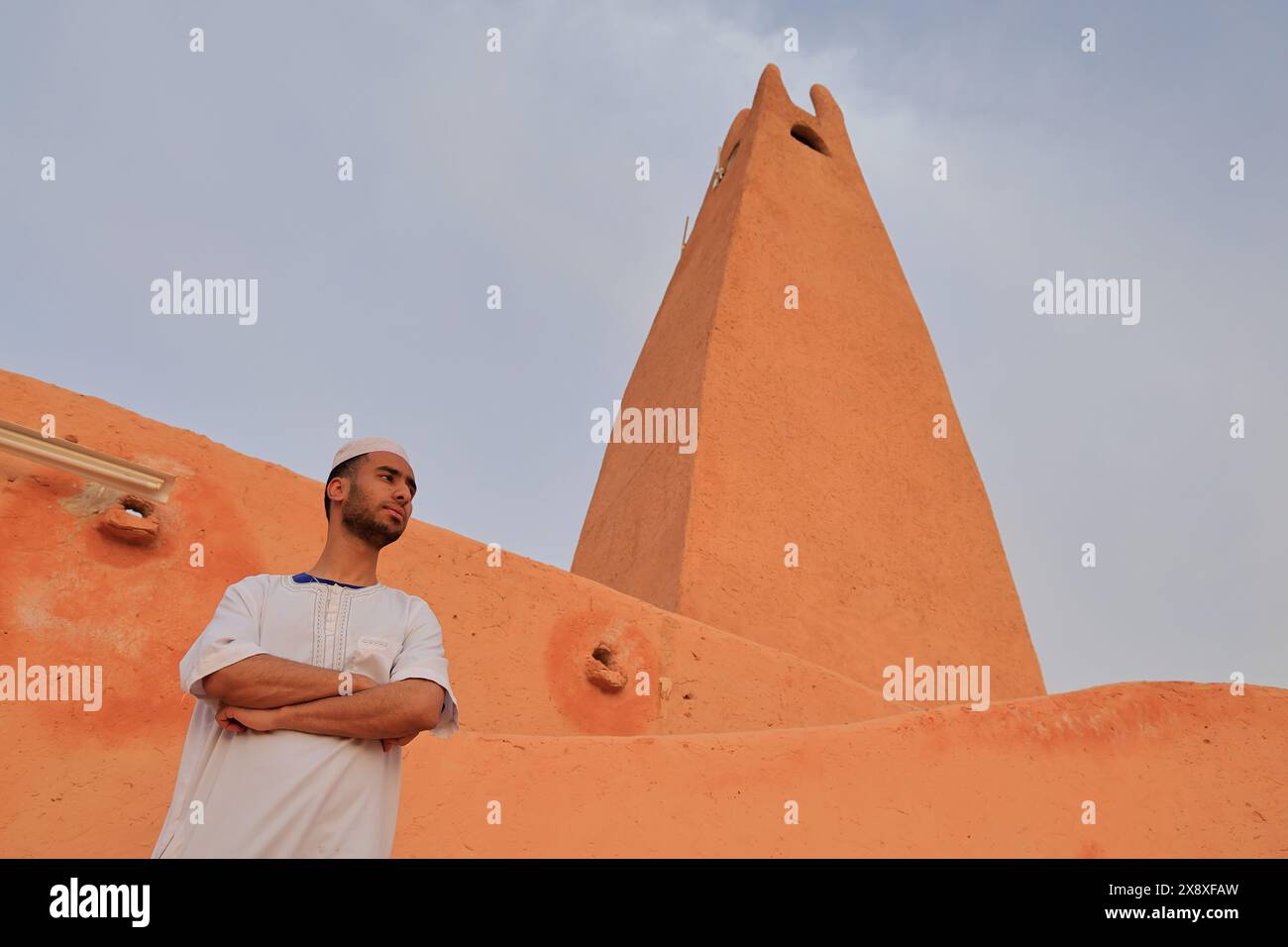 A man in traditional outfit in front of the minaret of the grand mosque ...